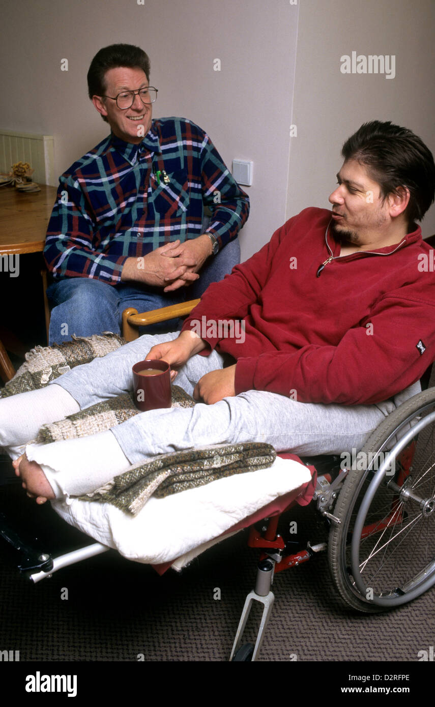 Young man in wheelchair chatting with helper in center Stock Photo - Alamy