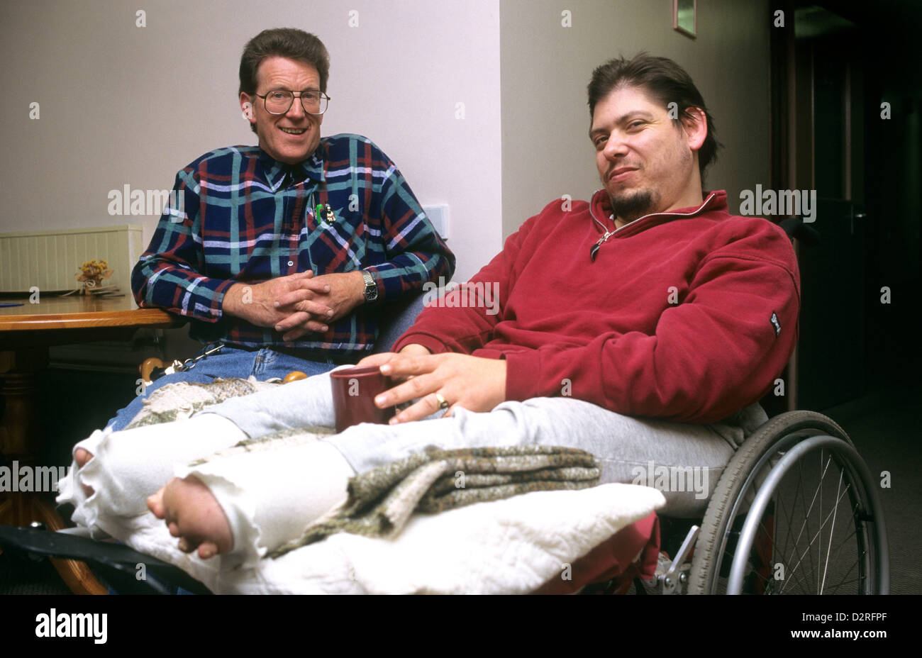 Young man in wheelchair chatting with helper in center Stock Photo - Alamy