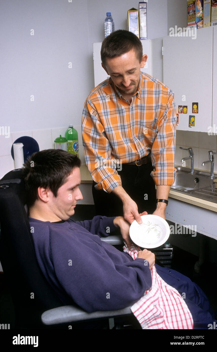 Young Disabled man being helped with kitchen chores of washing and ...