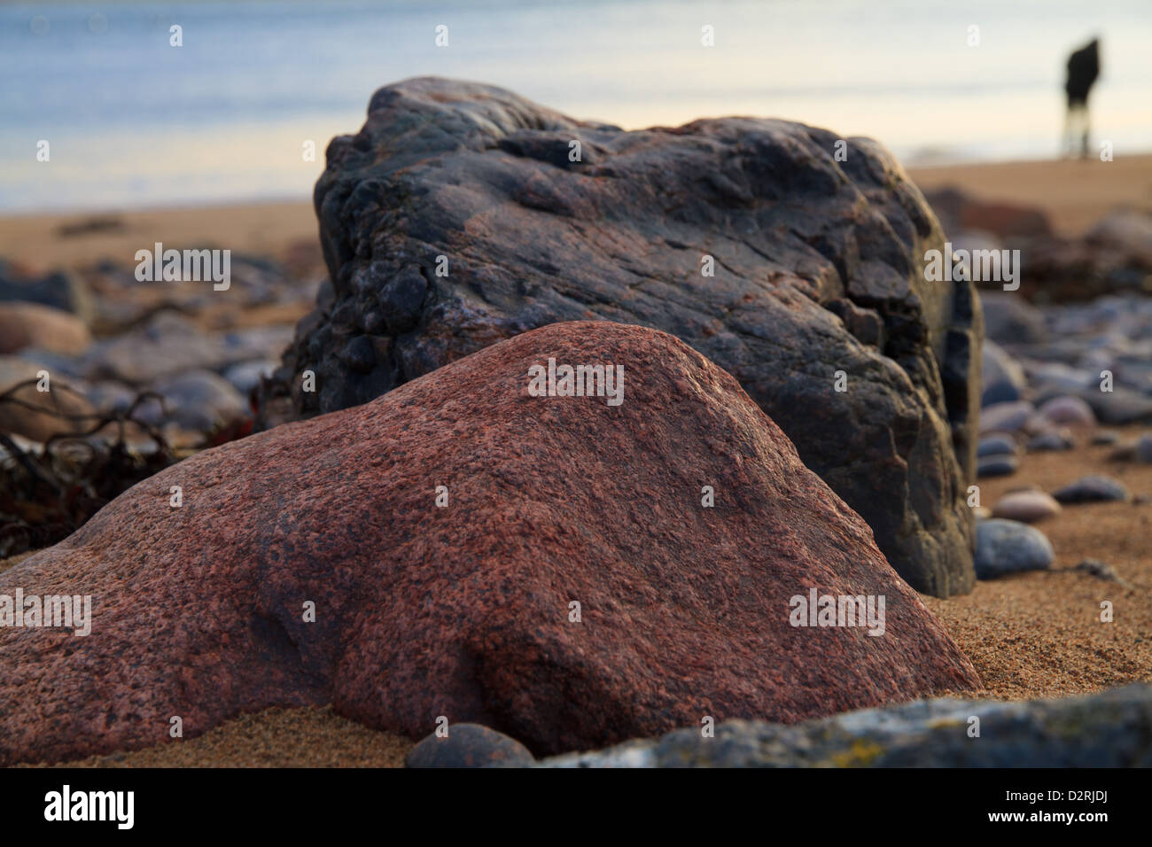 Close up image of two large rocks on a sandy and pebbly beach with a ...
