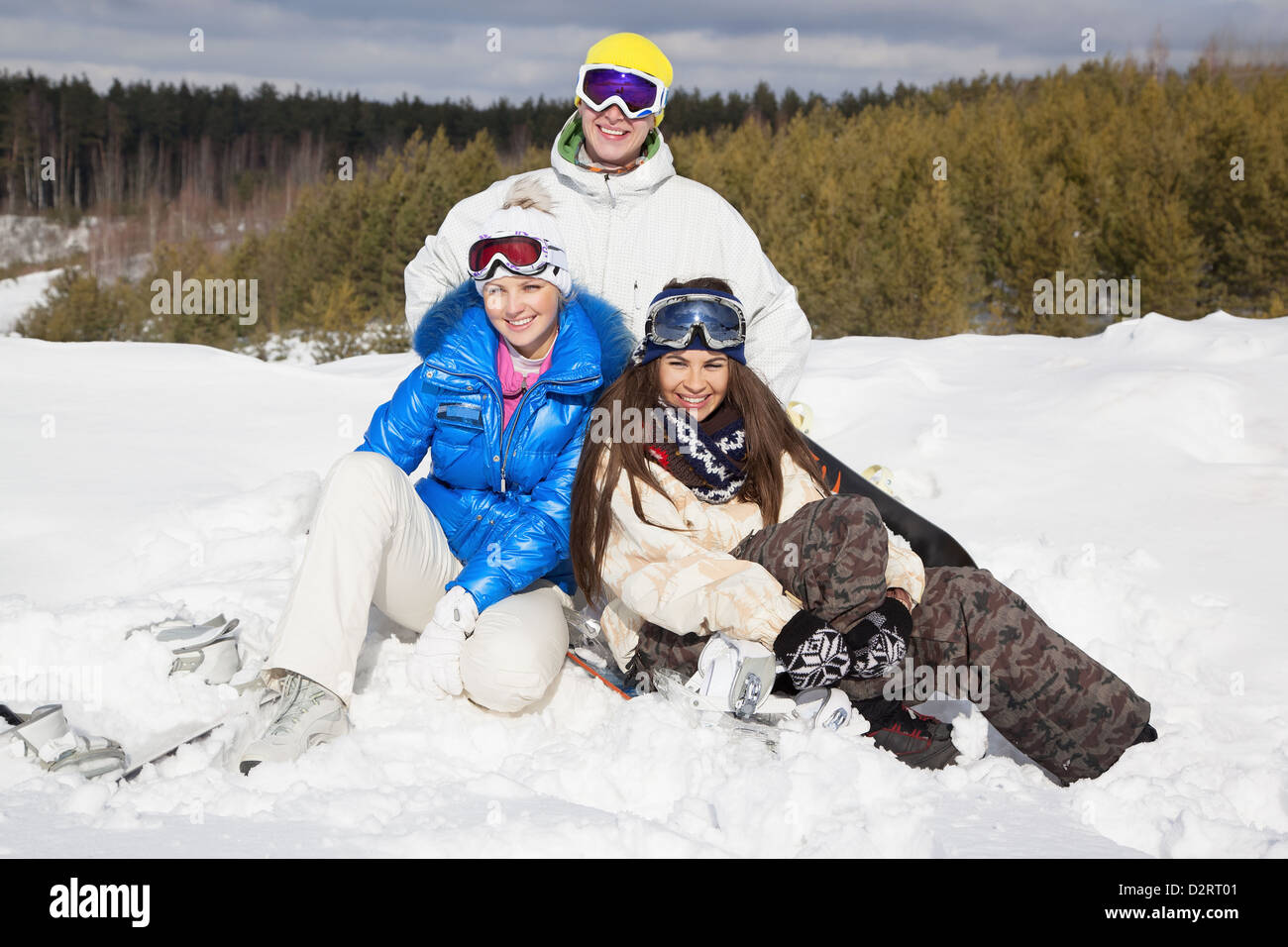 Group of young people sitting on the snow and smiling, sunny winter day ...