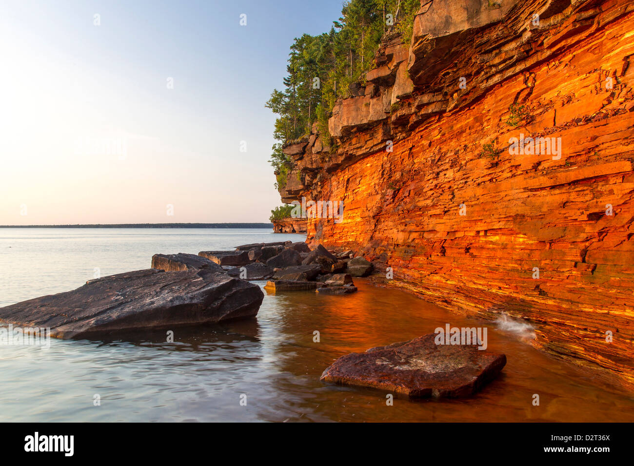 Layered sandstone cliffs and sea caves at sunrise on Devils Island in ...