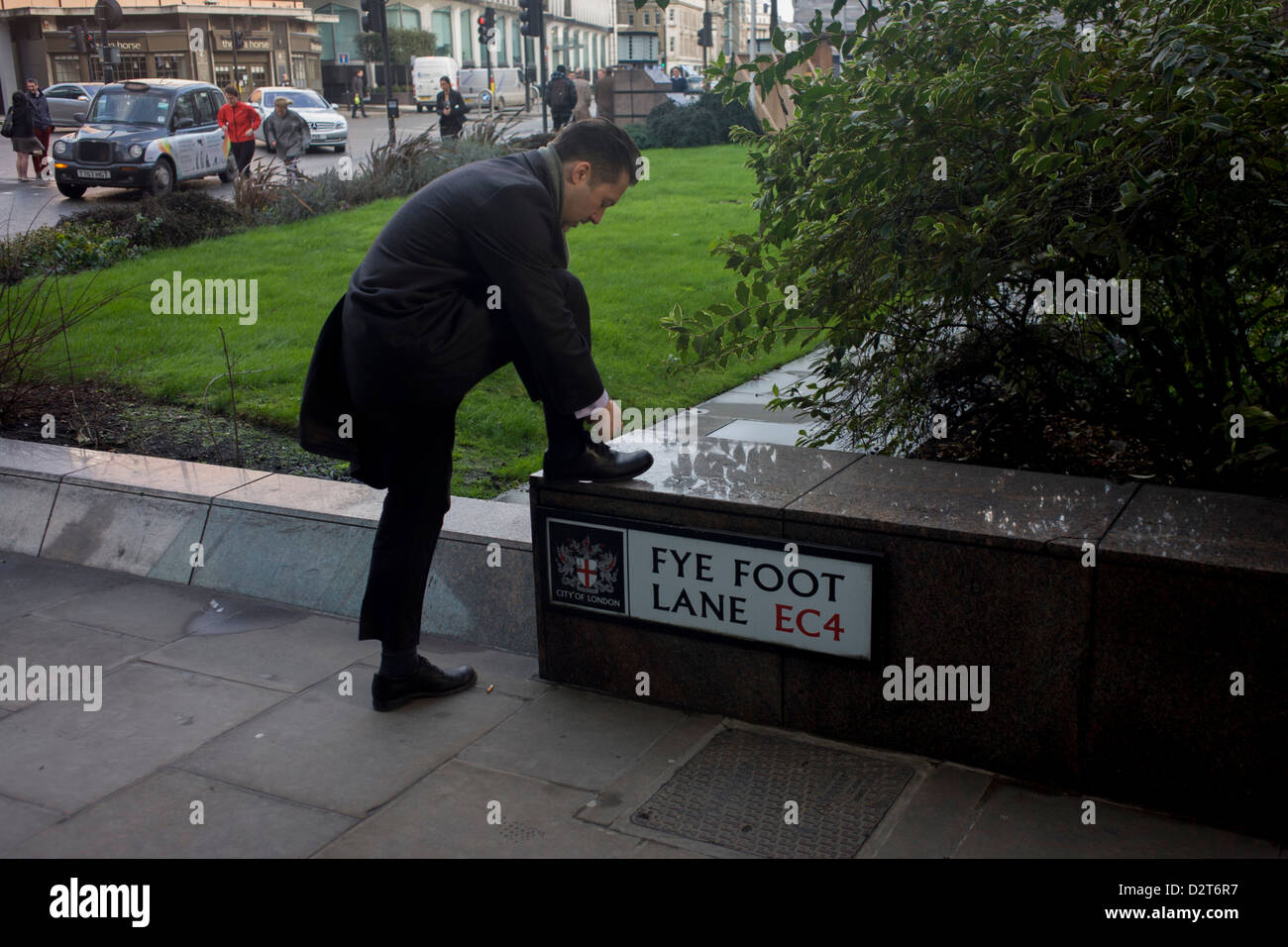 A businessman stoops down to tie a shoelace, resting his leg in Fye ...