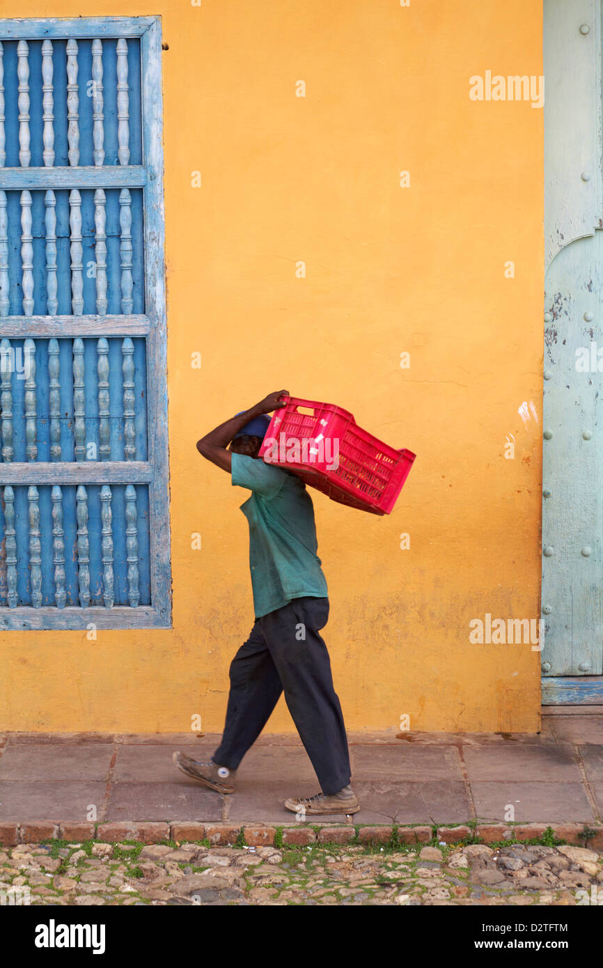 Daily life in Cuba - Cuban man walking down street carrying red crate ...