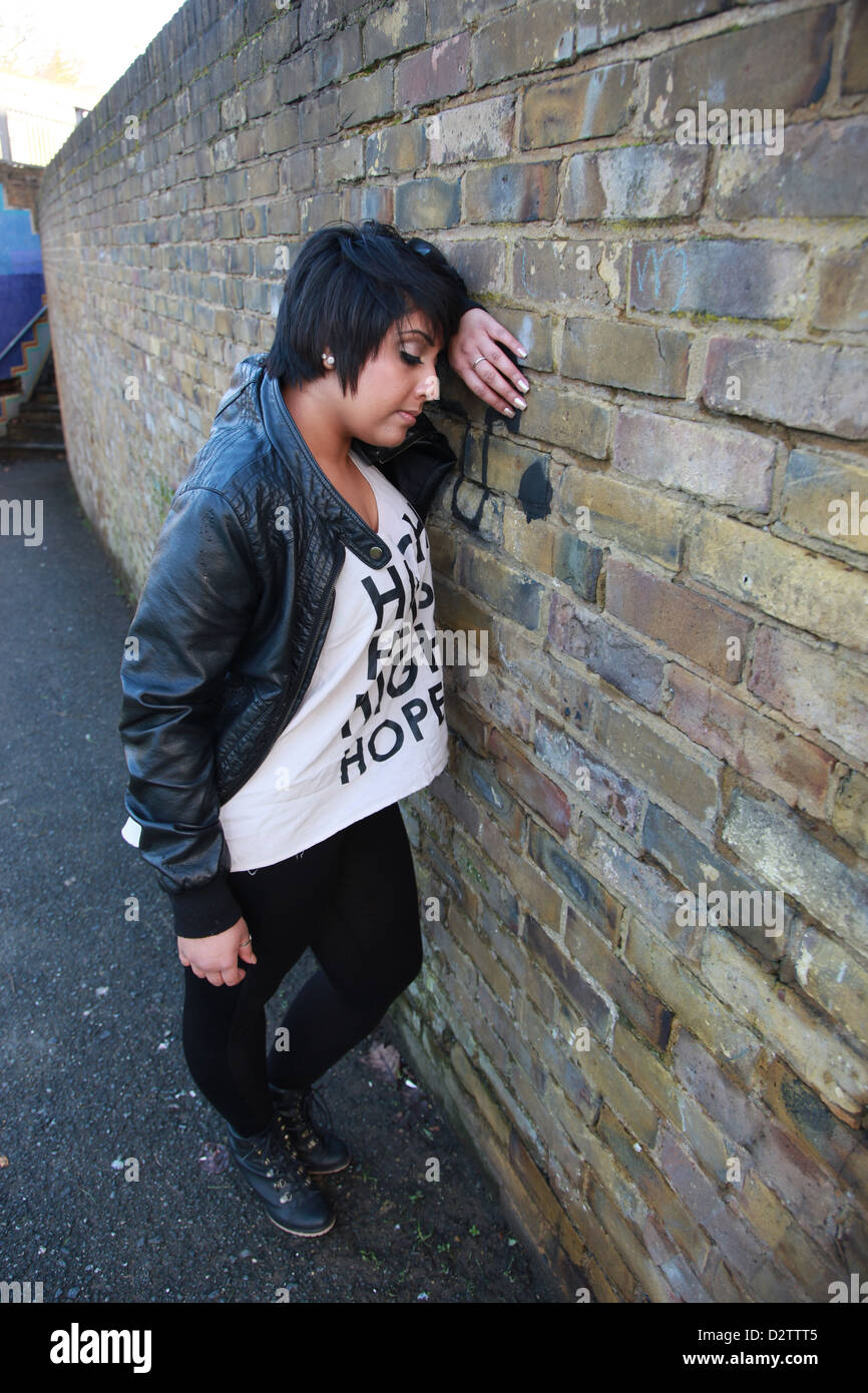 Upset and scared Asian girl leaning against a brick wall Stock Photo ...