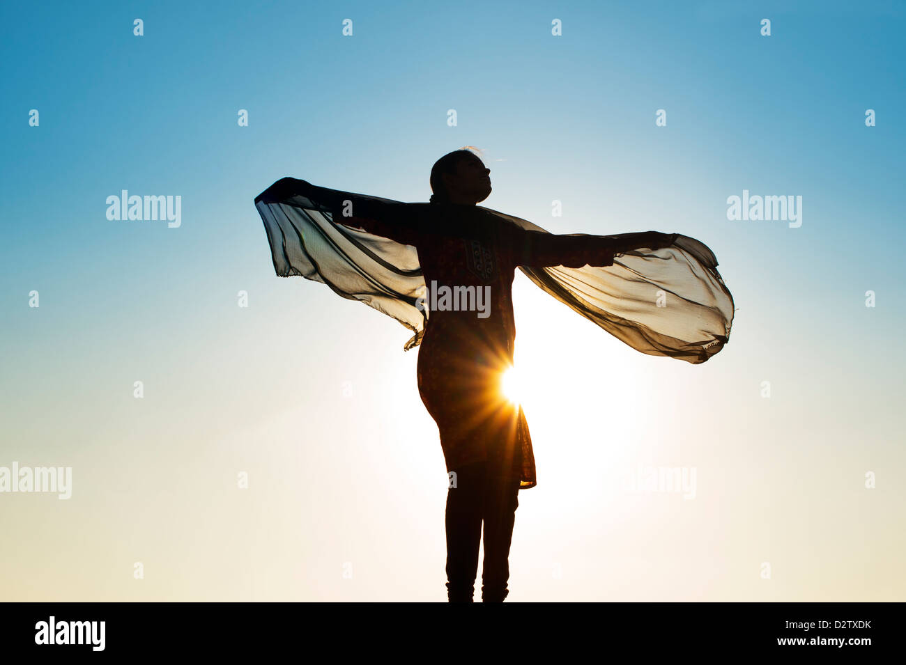 Indian girl with a veil turning in the wind towards the sun. Silhouette ...