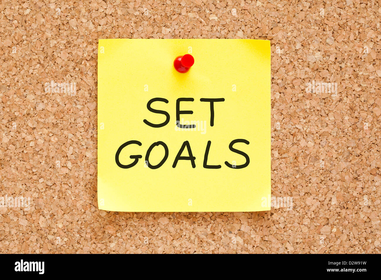 Set Goals on yellow sticky note pinned with red push pin on cork board ...
