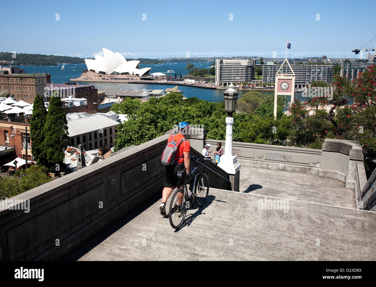 Solo cyclist carries his bicycle down the steps with the Sydney Opera ...