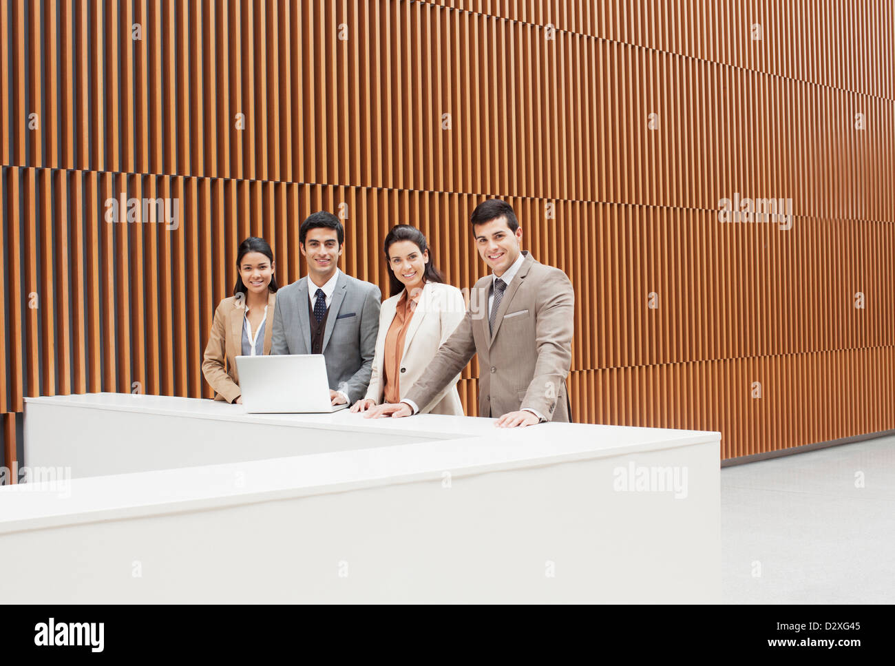 Portrait of confident business people with laptop at ledge in office ...