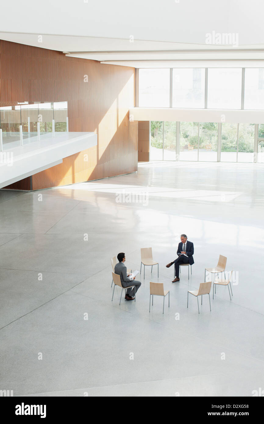 Businessmen sitting at circle of chairs in modern lobby Stock Photo - Alamy