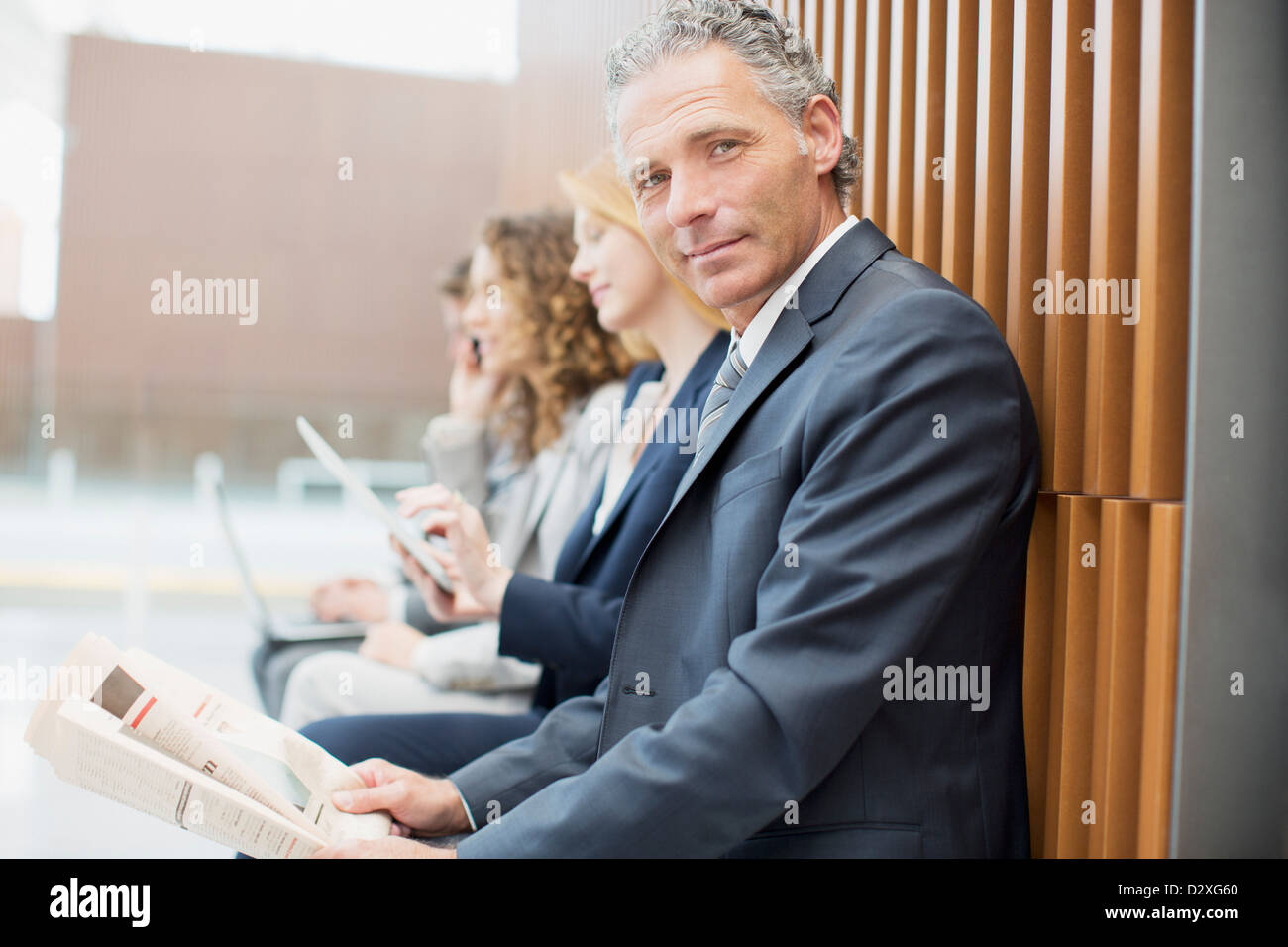 Portrait of confident businessman reading newspaper with co-workers in ...
