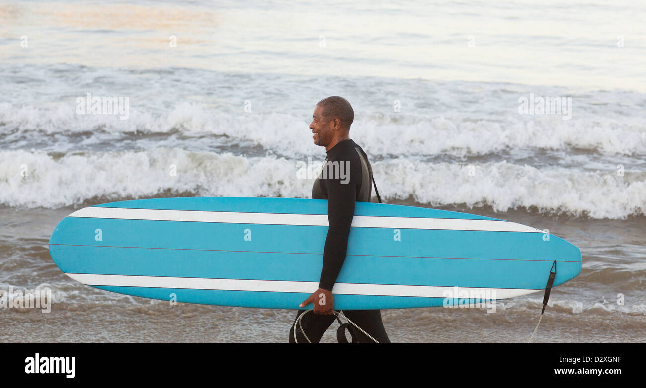 Older surfer carrying board on beach Stock Photo - Alamy
