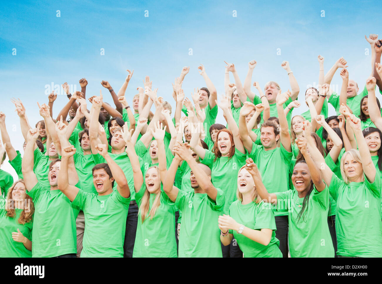 Crowd in green t-shirts cheering with arms raised Stock Photo - Alamy