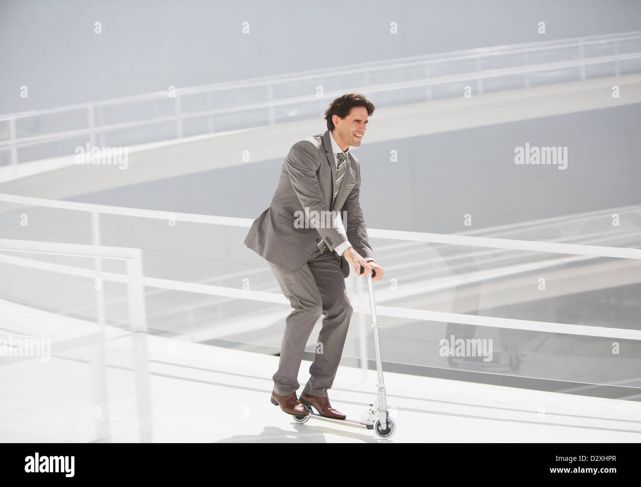 Businessman riding scooter down walkway Stock Photo - Alamy
