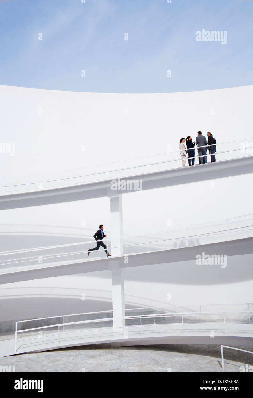 Businessman running up elevated walkway toward business people Stock ...