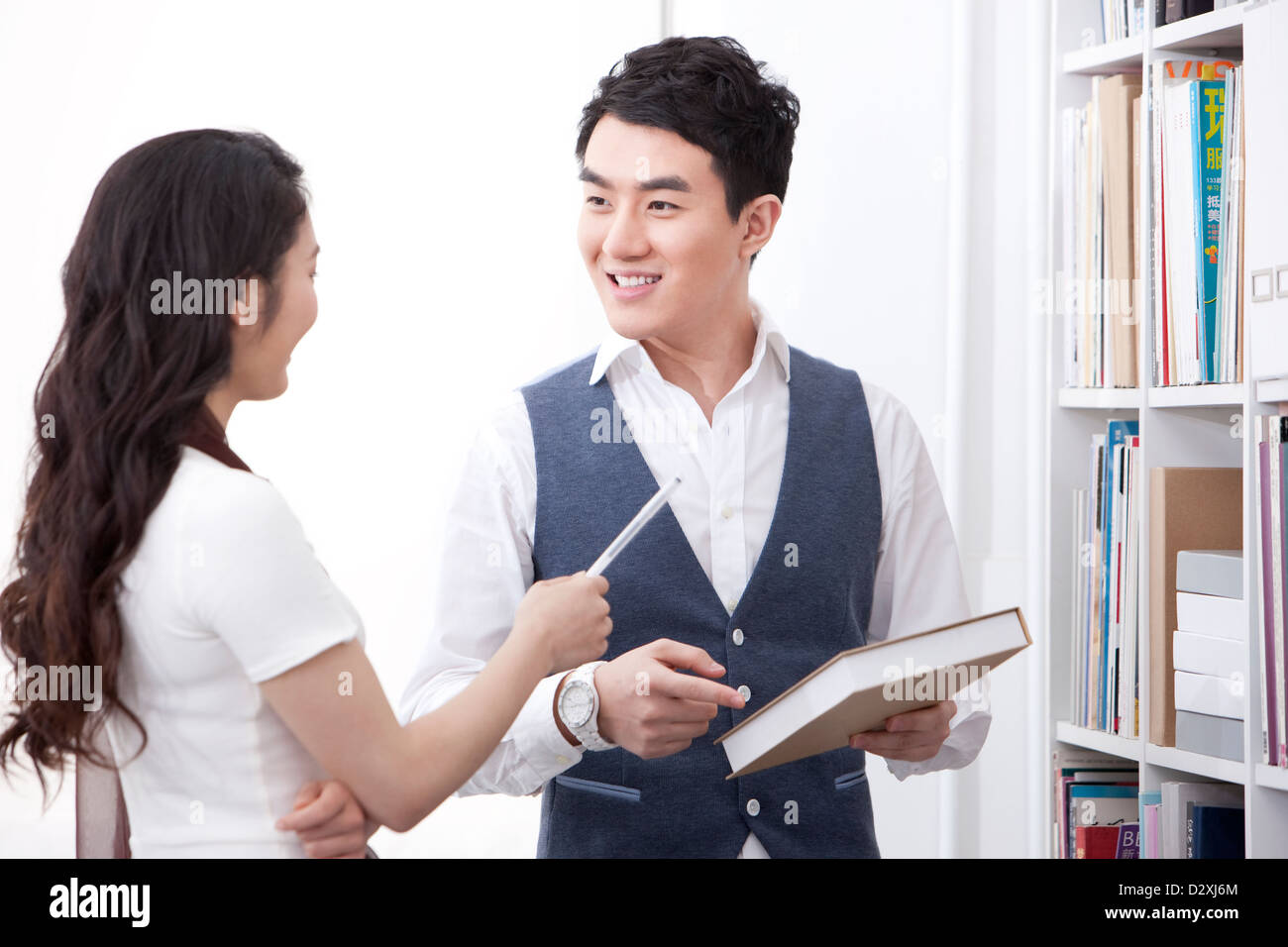 Happy office workers talking in front of book shelf Stock Photo - Alamy
