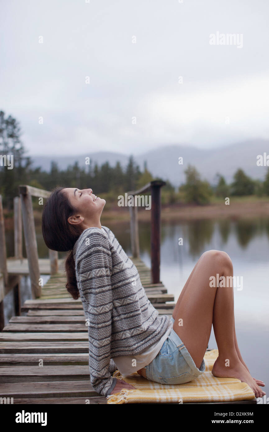 Smiling woman sitting on dock at lakeside with head back Stock Photo ...