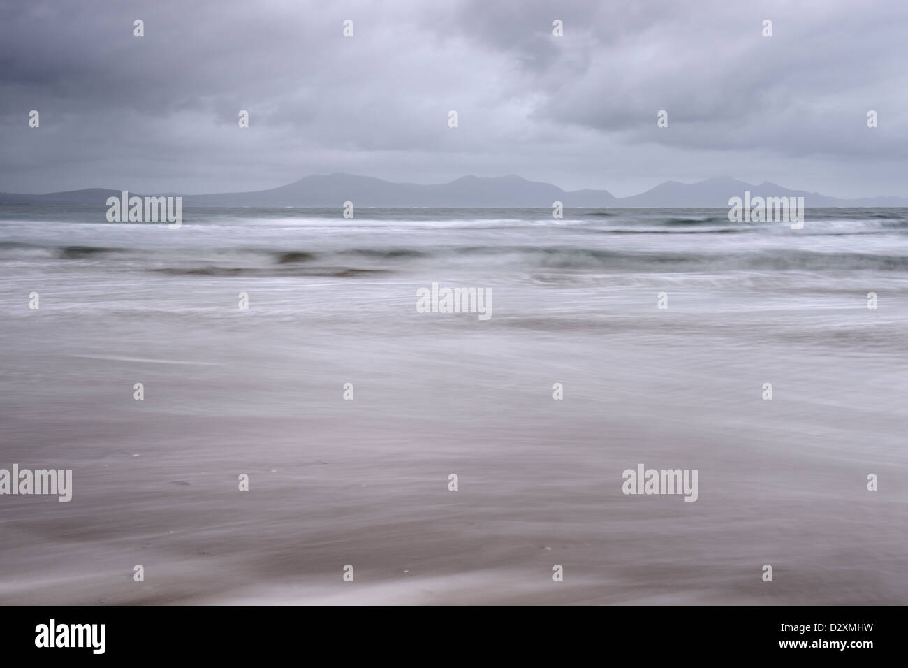 Waves washing over Newborough Beach with dark clouds looming above the ...