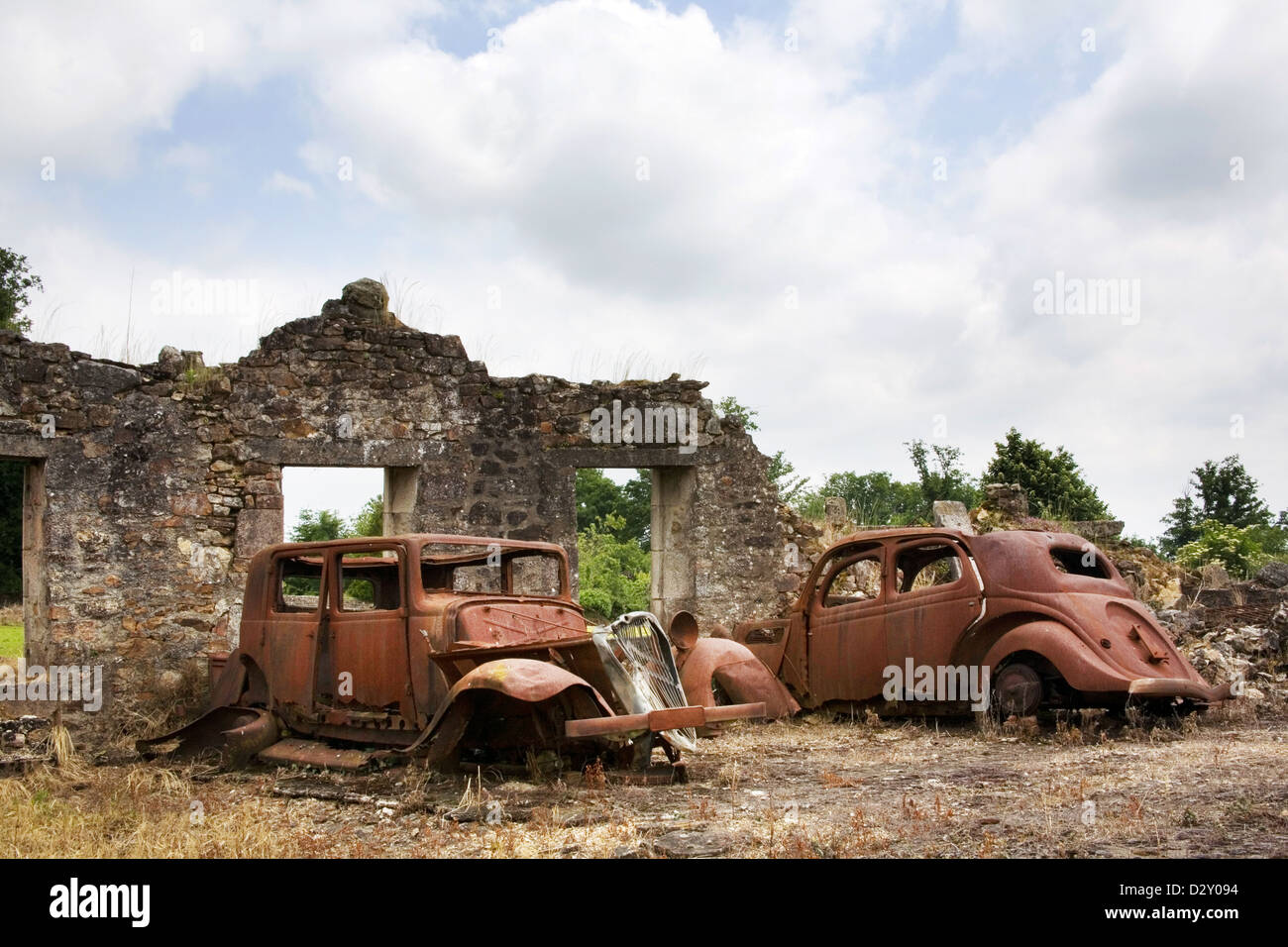 Two burnt out cars that are very rusty in a destroyed building, the ...