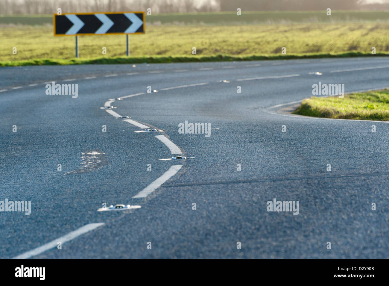 An empty bend in a road with white lines and chevron signs in side ...