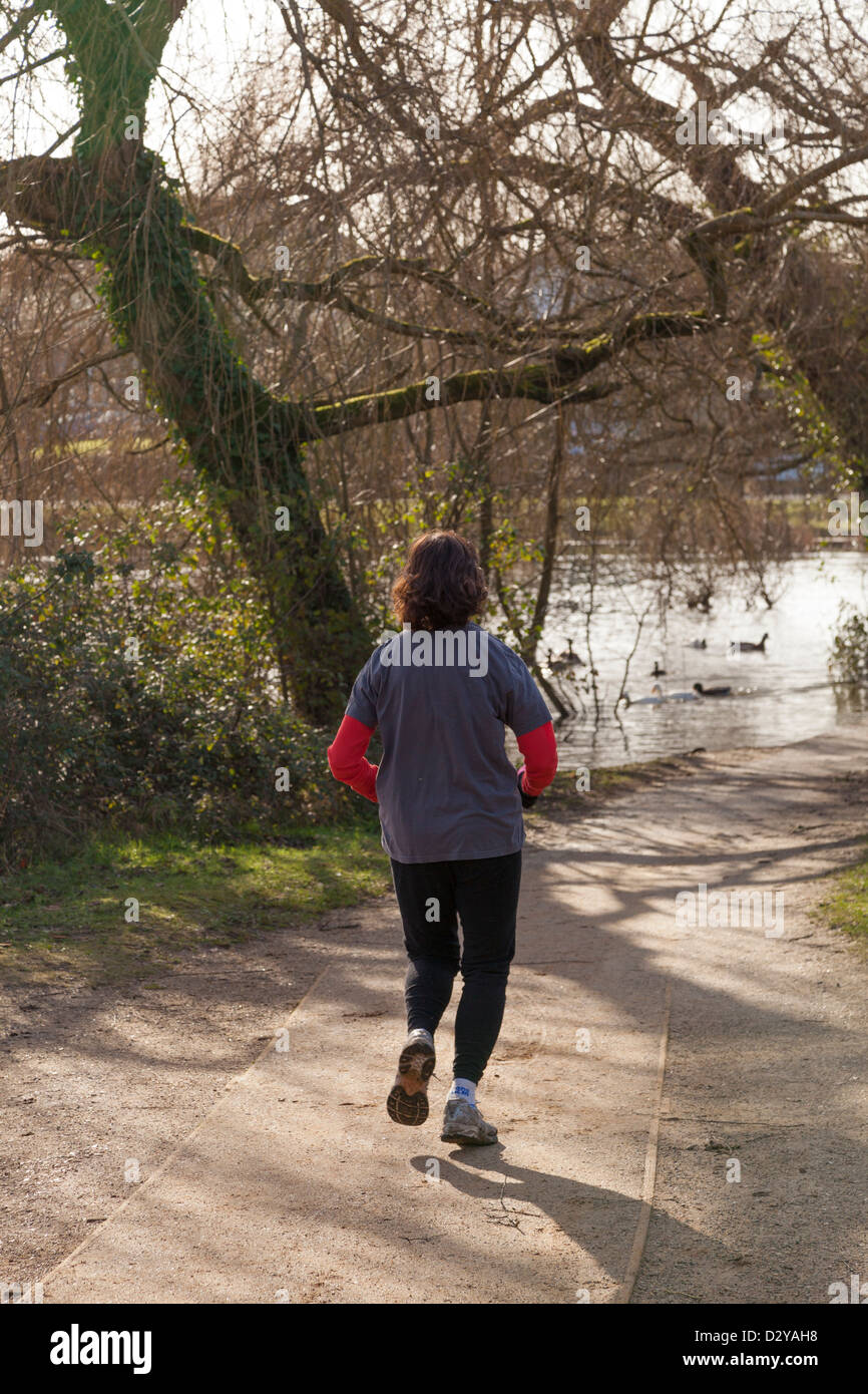 back view of female jogger on path by lake in winter sunshine Stock ...
