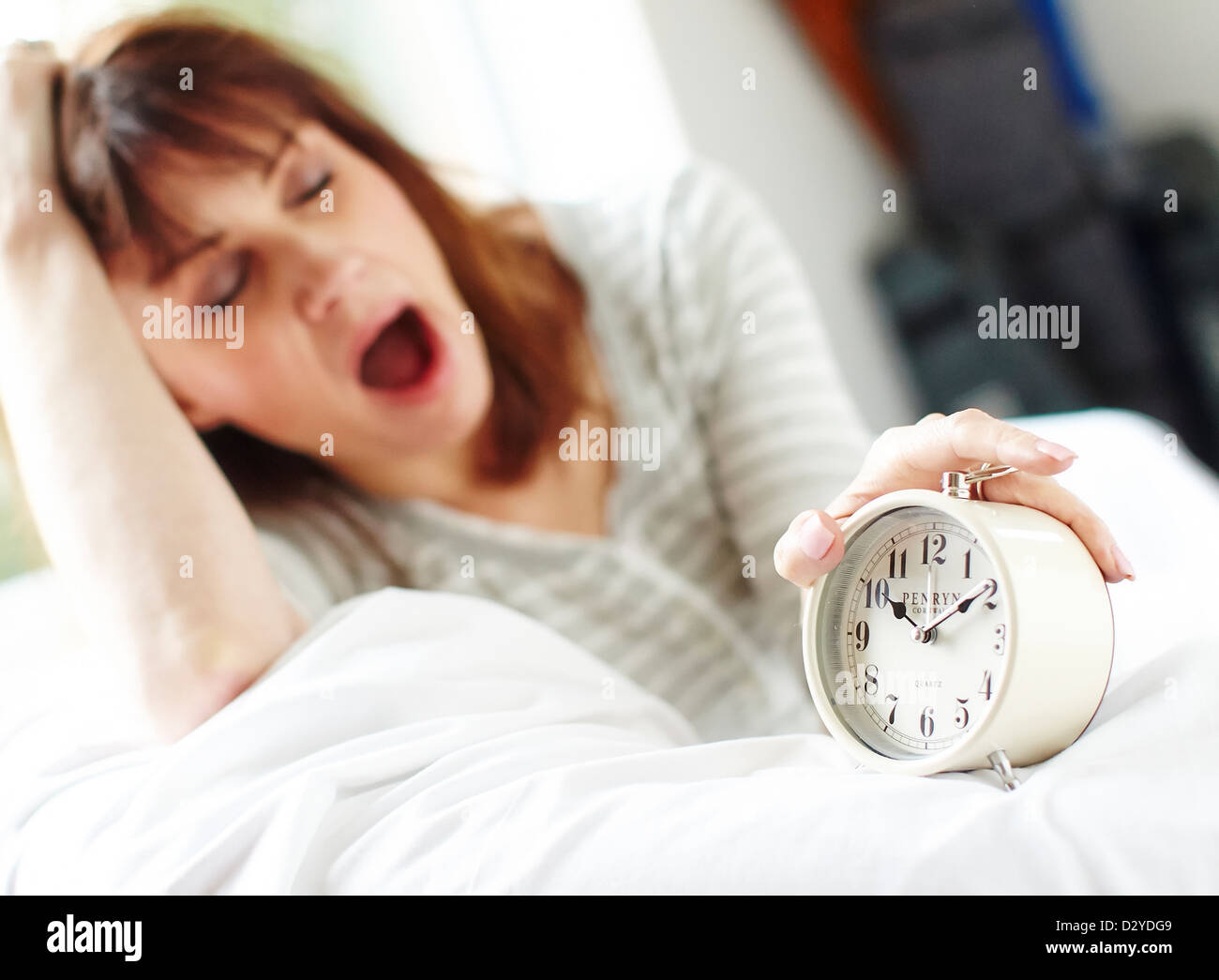 Woman tired looking at alarm clock Stock Photo - Alamy