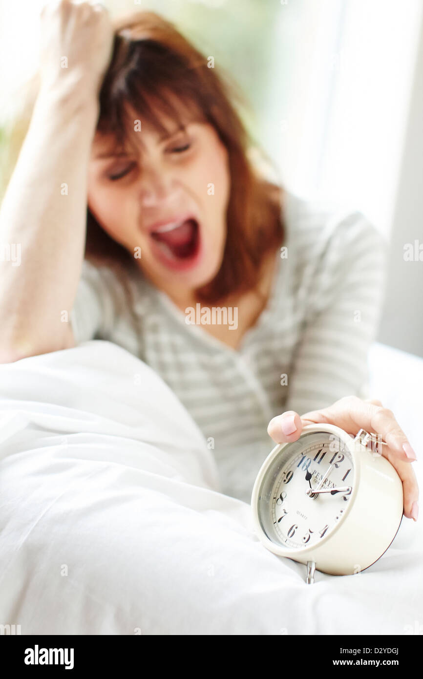 Woman tired looking at alarm clock Stock Photo - Alamy