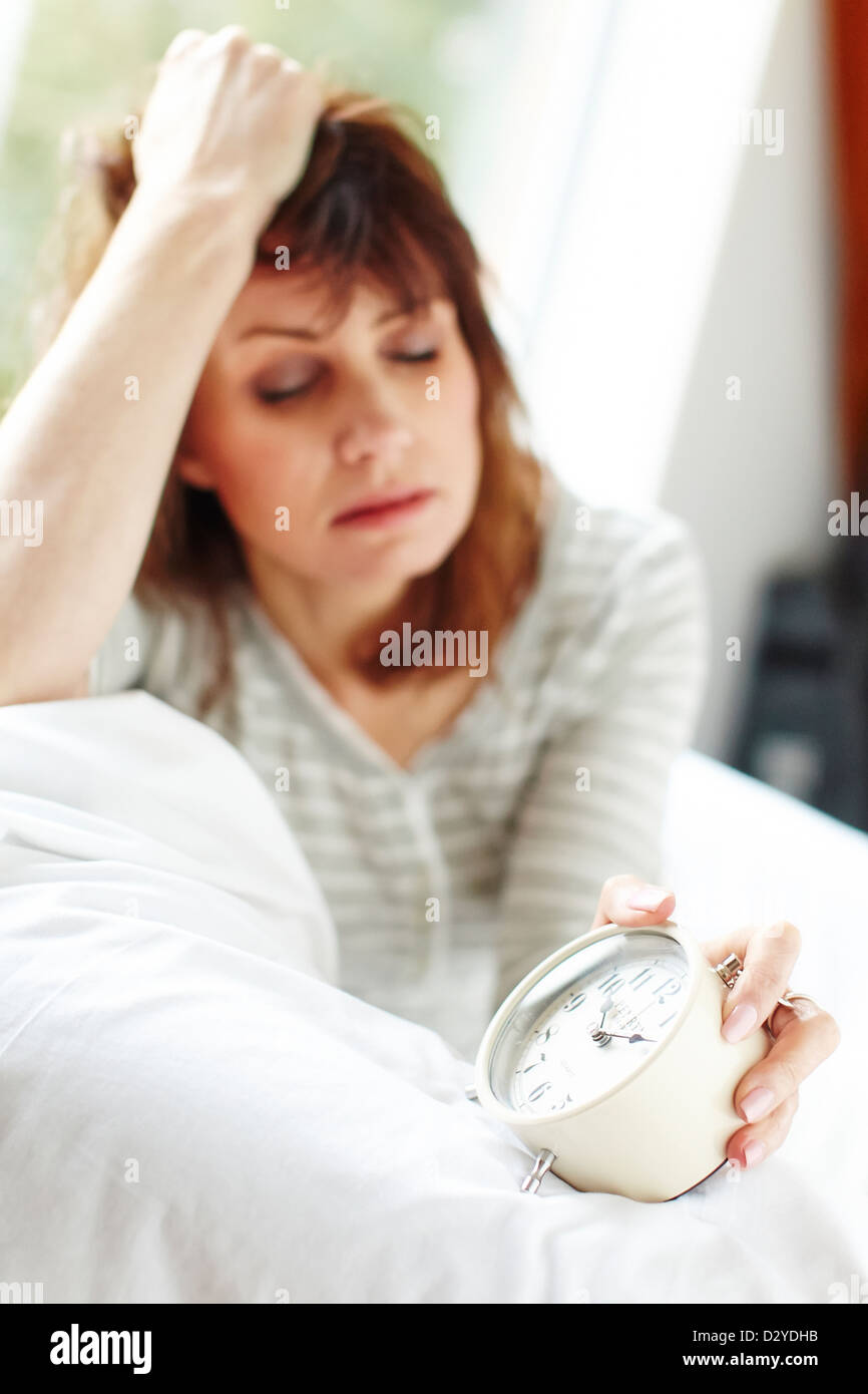 Woman tired looking at alarm clock Stock Photo - Alamy