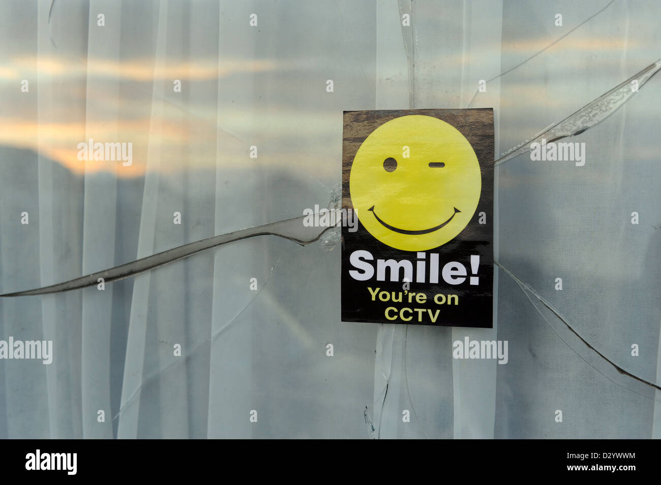 A 'Smile! You're on CCTV' sticker on a broken window Stock Photo - Alamy