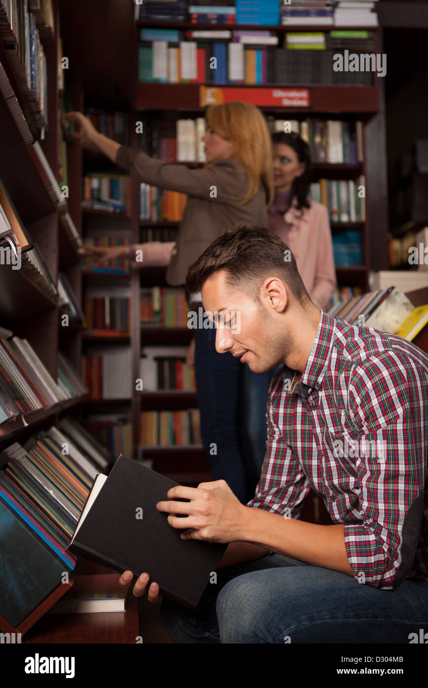 young caucasian handsome guy in a bookshop reading a book with other ...