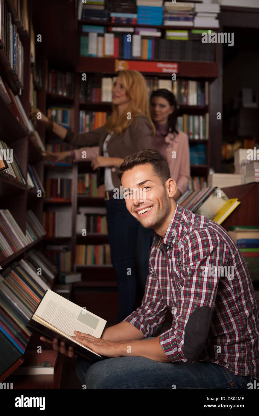 young caucasian handsome guy in a bookstore smiling with an opened book ...