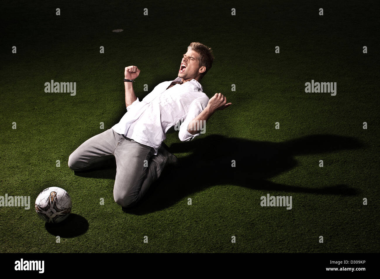 Footballer shouting and kneeling on pitch Stock Photo - Alamy