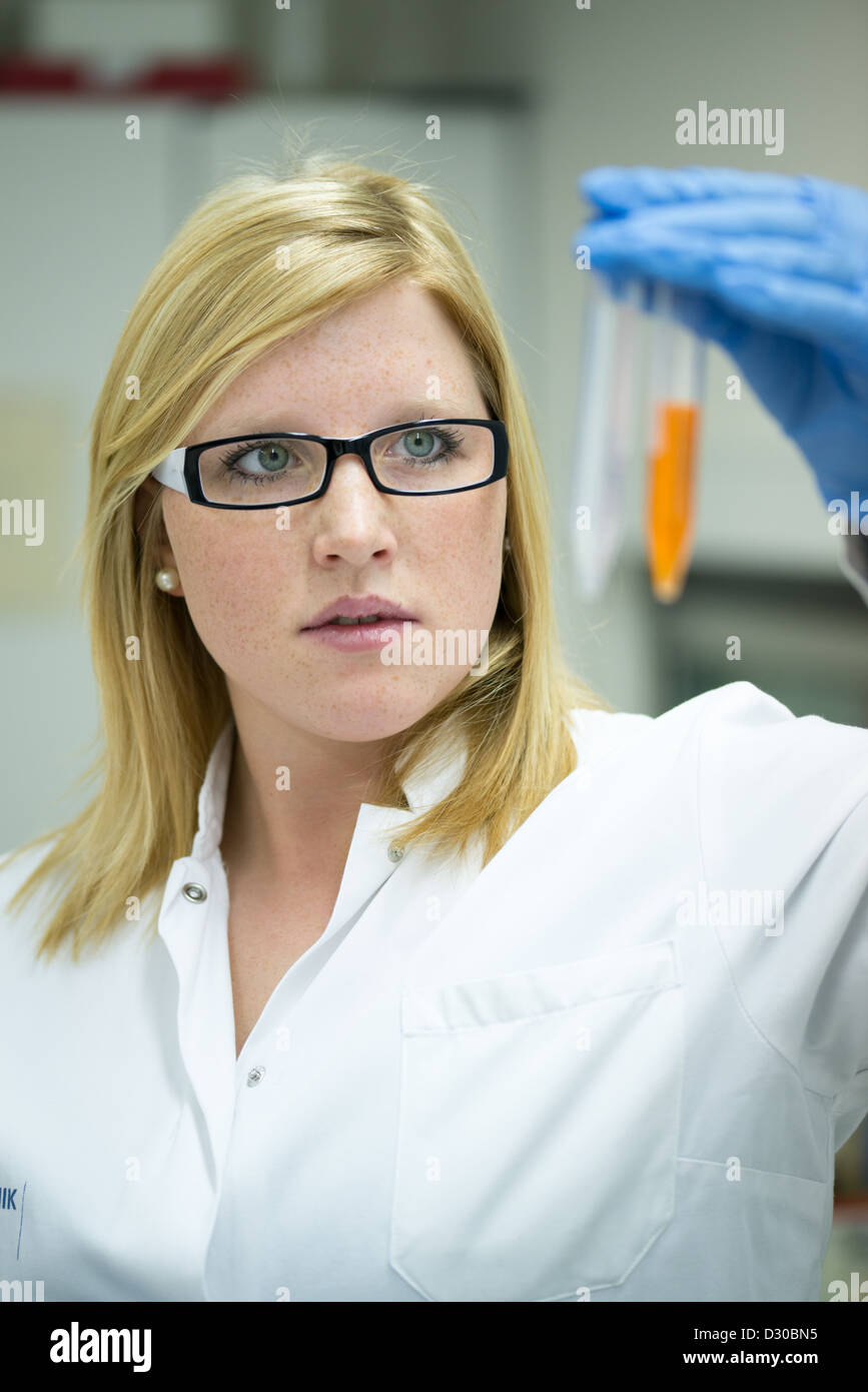Young female scientist in university laboratory looking at flask with ...
