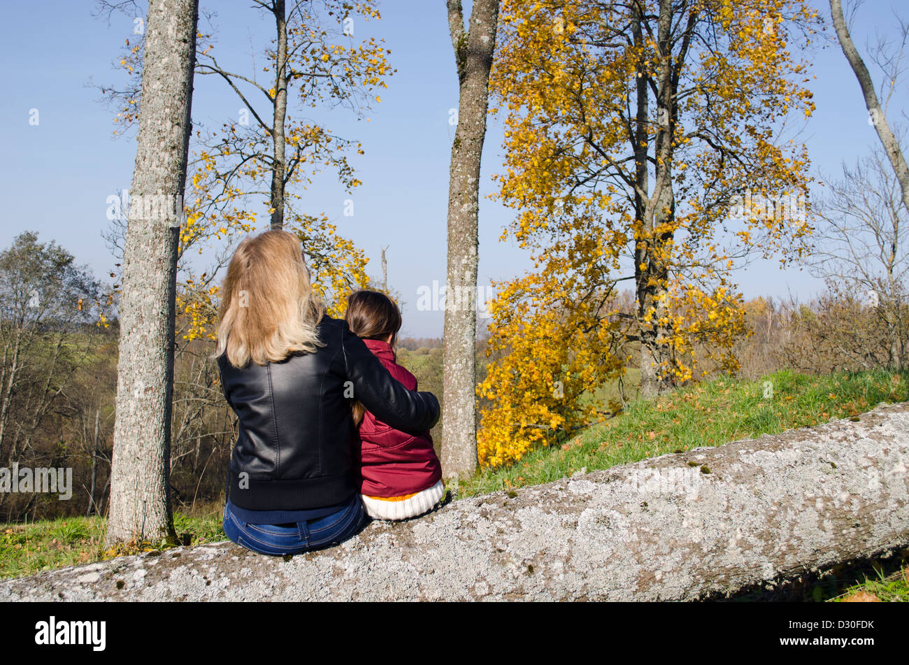 blond woman mother sit on broken tree trunk with her daughter admire ...