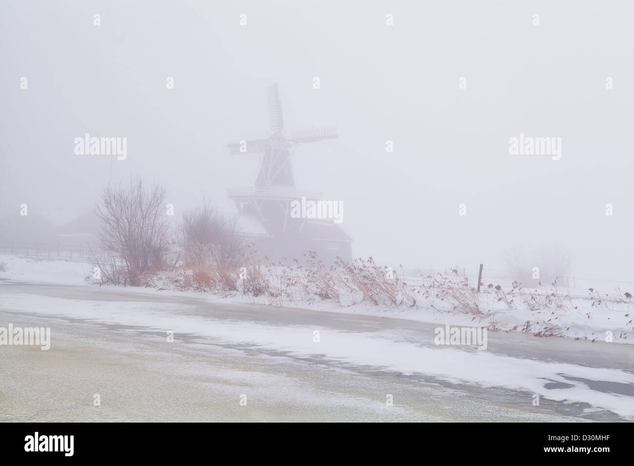 Dutch windmill by frozen canal in dense fog Stock Photo - Alamy