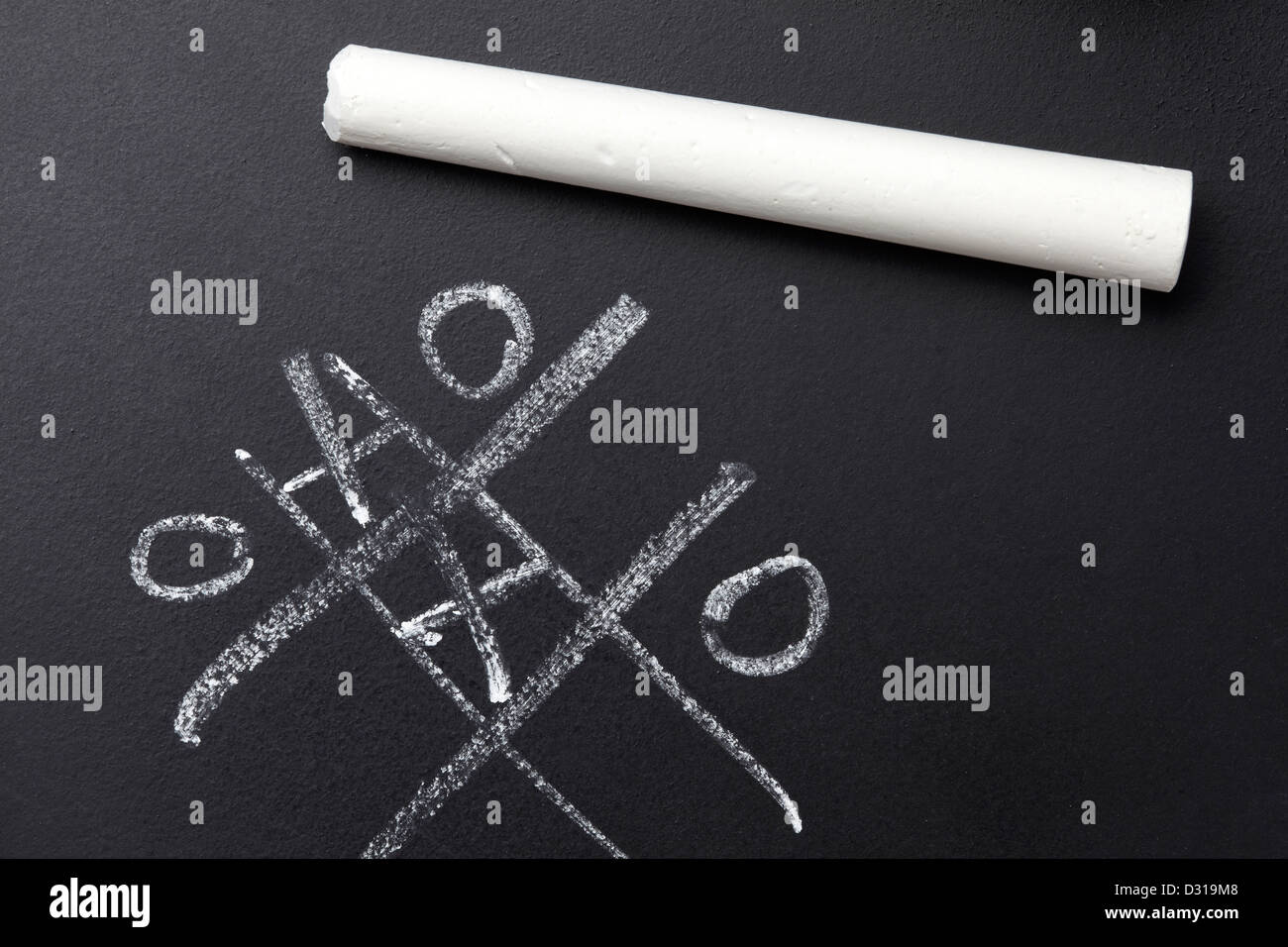 White chalk resting on black board with nought and crosses game Stock ...