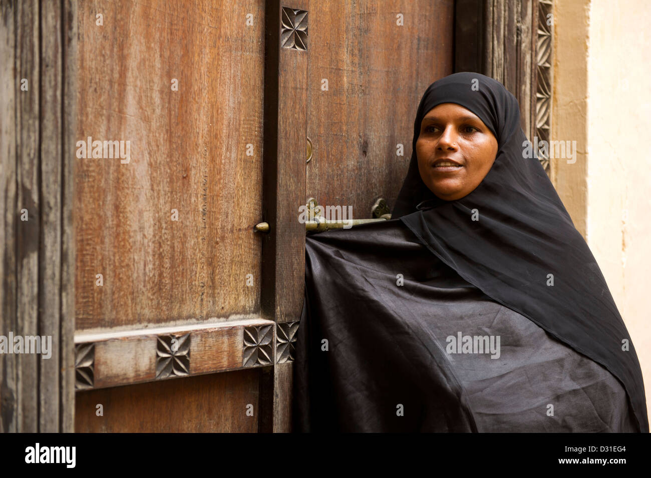 Swahili woman standing at a traditional Zanzibar door in the old fort ...