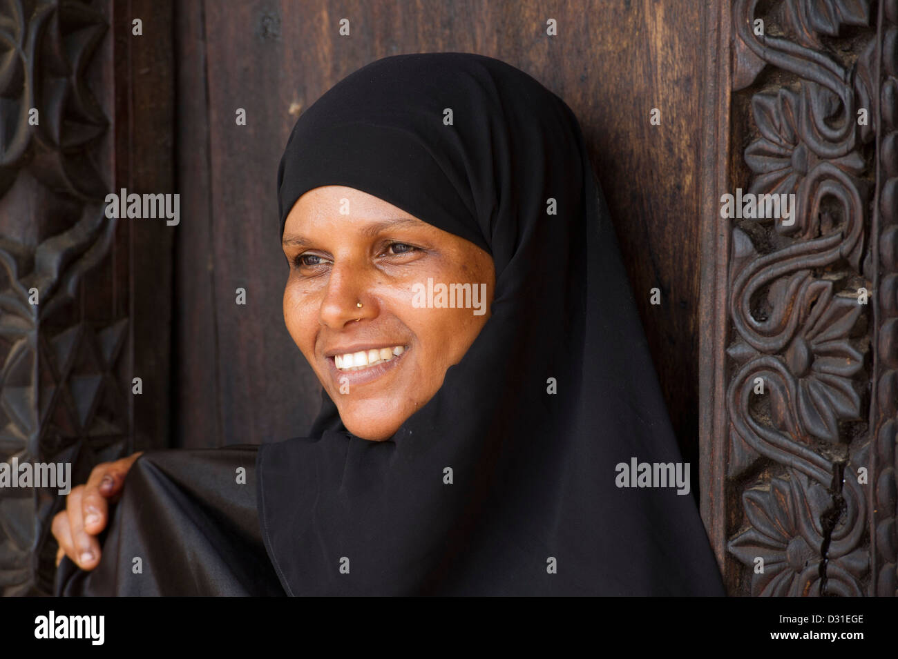 Swahili woman standing at a traditional Zanzibar door in the old fort ...