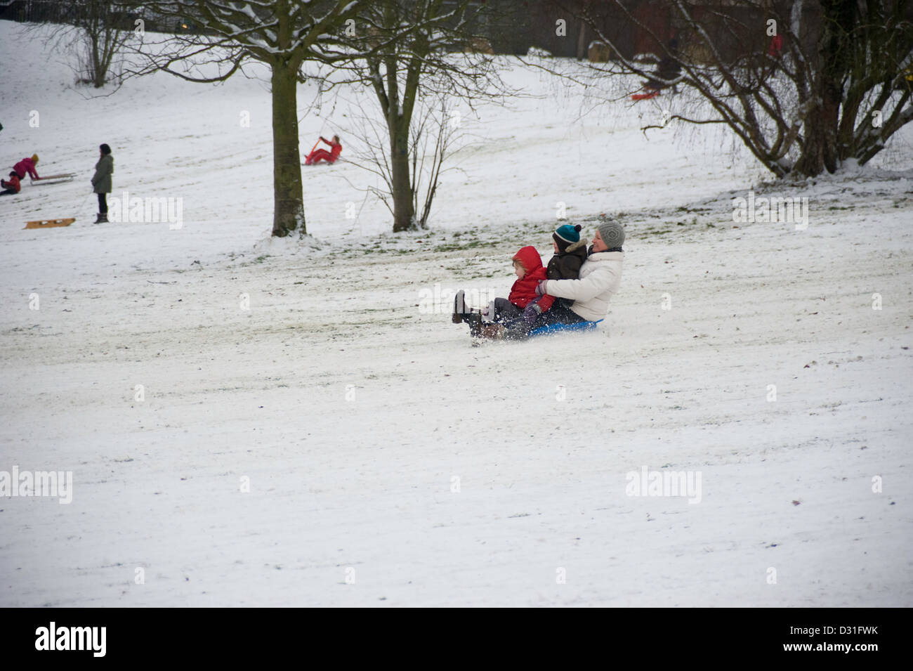 An adult and two children on a toboggan in the snow Stock Photo - Alamy