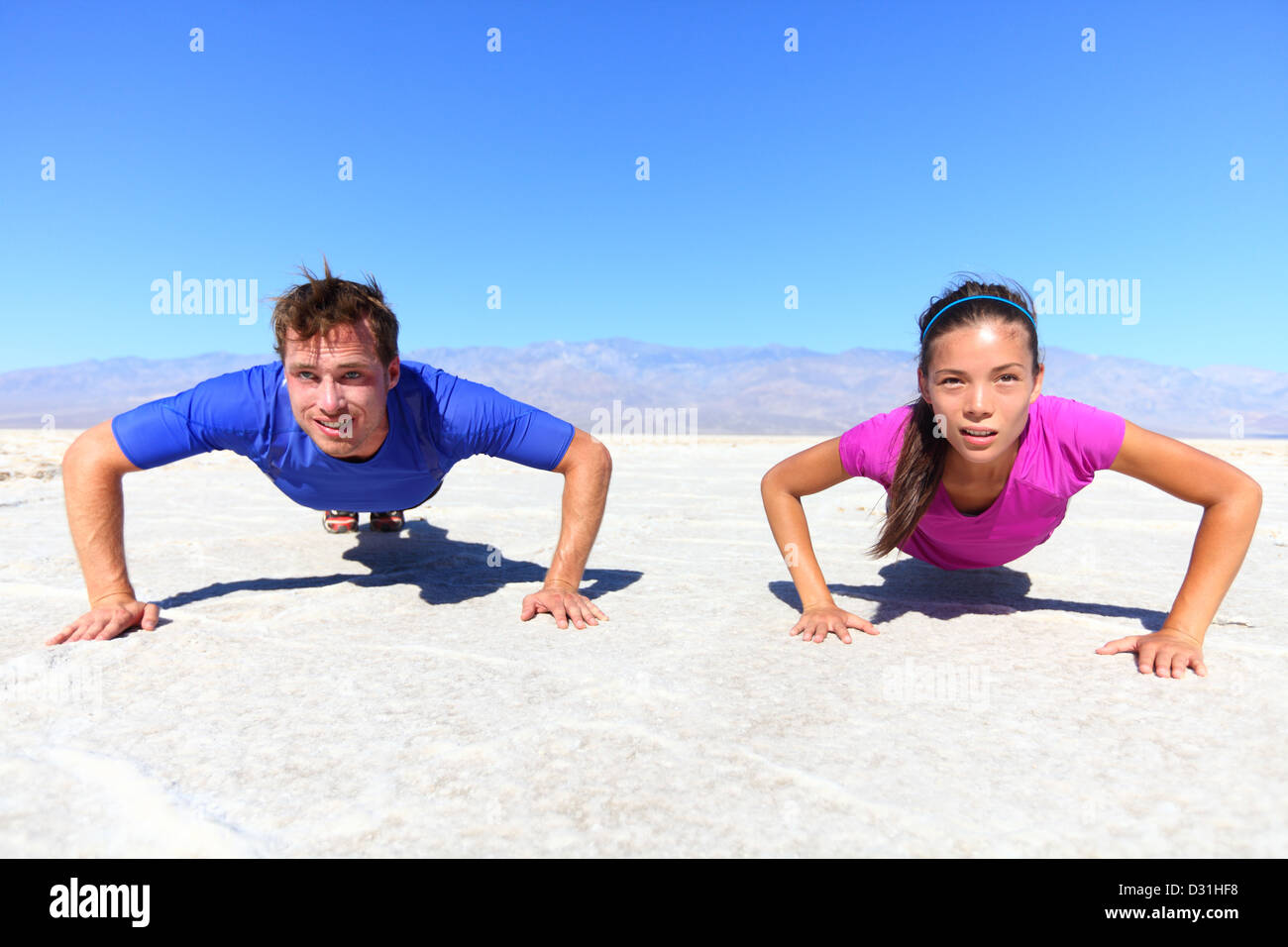 Young fitness couple doing push-ups exercise under the burning sun in ...