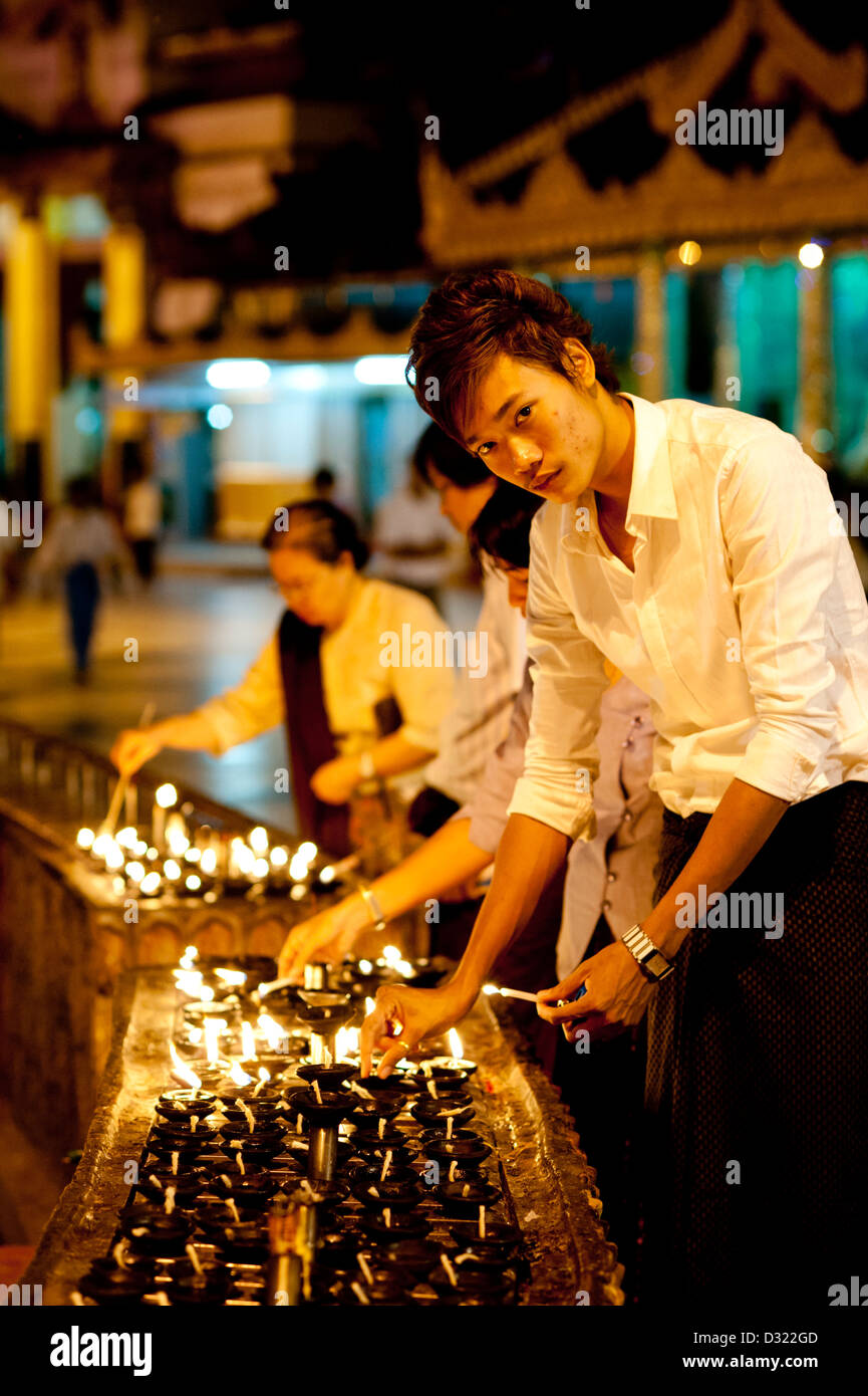 A young man lights oil lamps in prayer at Shwedagon Pagoda, Yangon ...