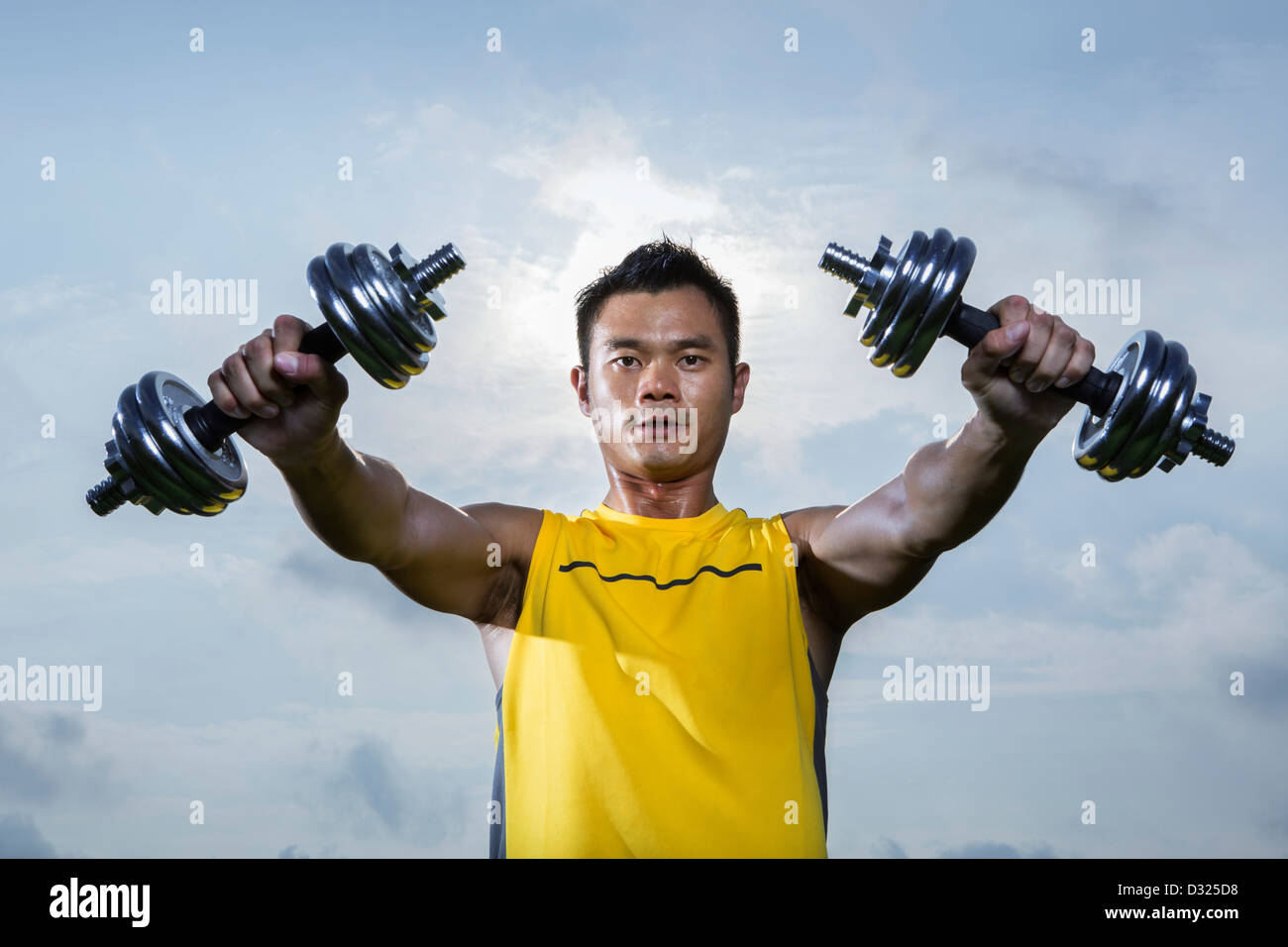 Athletic Young Chinese man exercising outdoors with dumbbells. Muscular ...