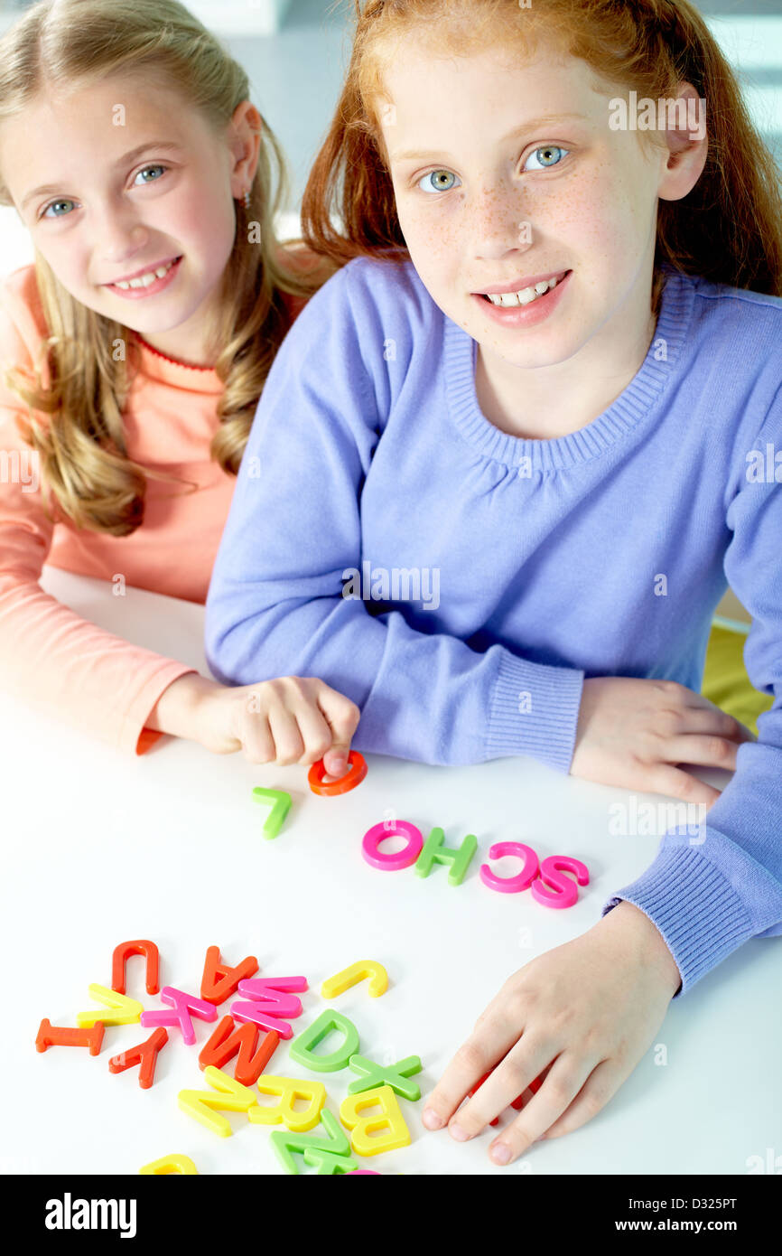 Portrait of smart girls making word ‘school’ and looking at camera ...