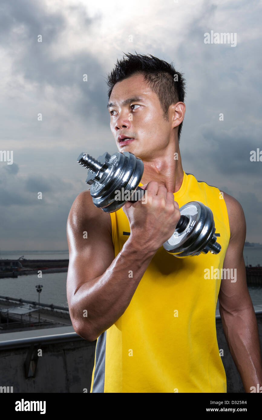 Athletic Young Chinese man exercising outdoors with dumbbells. Muscular ...