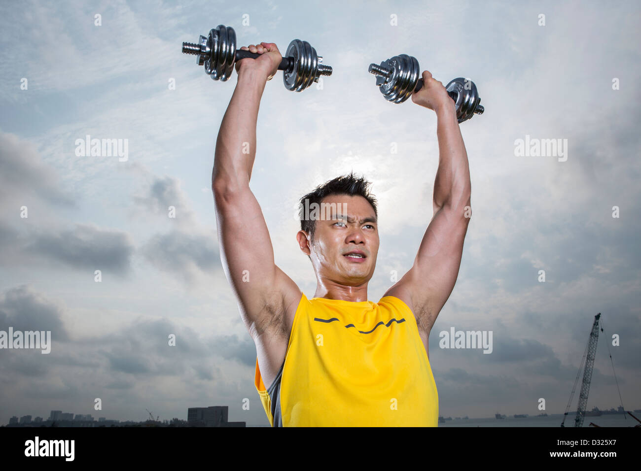 Athletic Young Chinese man exercising outdoors with dumbbells. Muscular ...