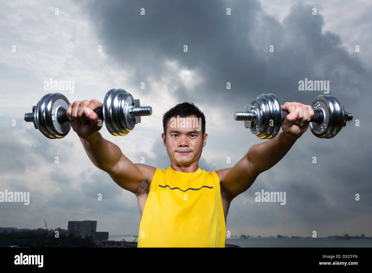 Athletic Young Chinese man exercising outdoors with dumbbells. Muscular ...