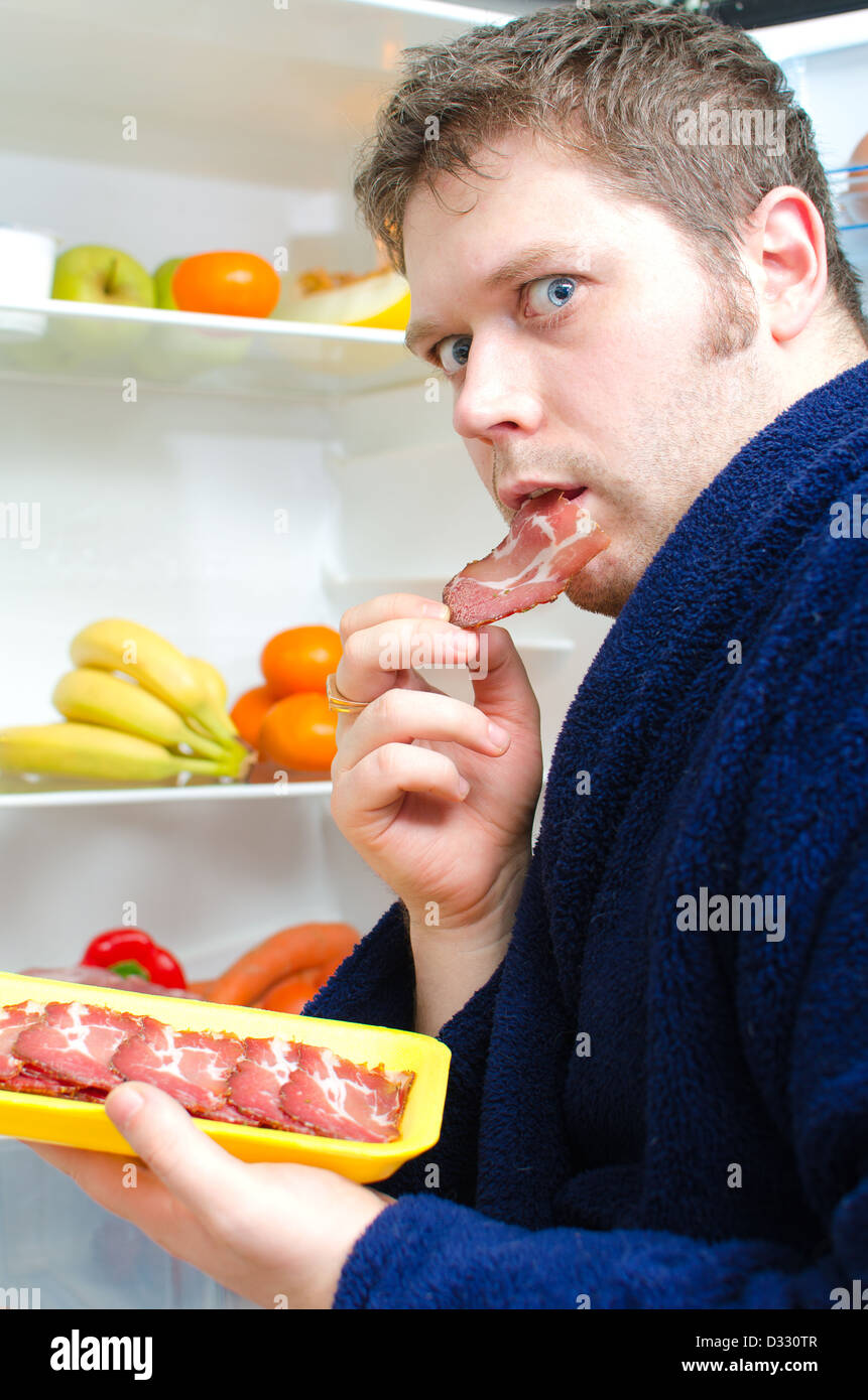 Handsome man eating ham slice near open fridge Stock Photo - Alamy