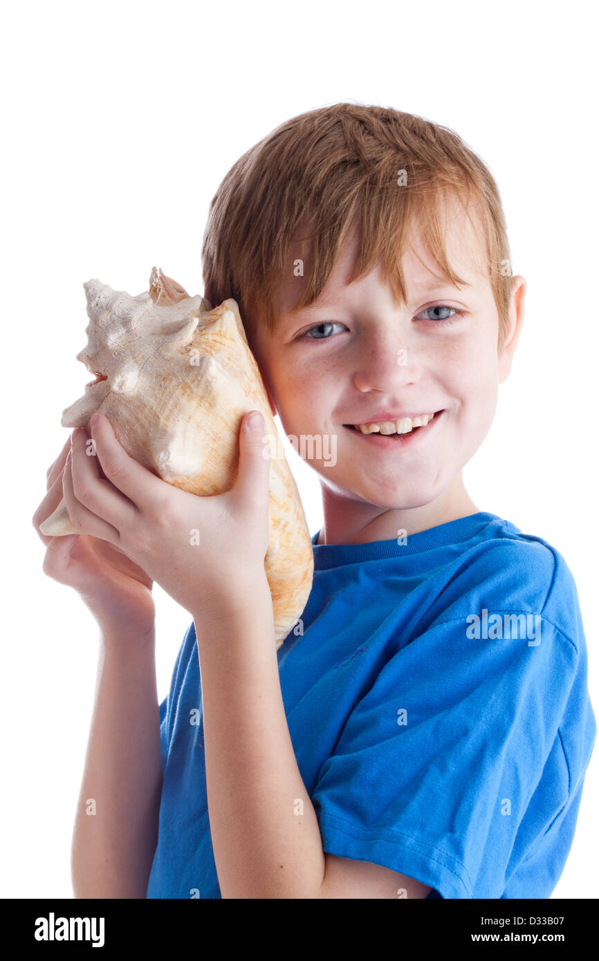 Bright smiling blue eyed boy 'listening to the sea' in large conch ...