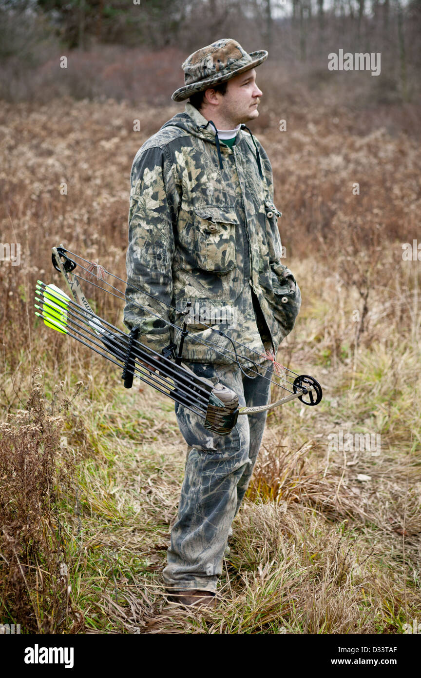 Man dressed in camouflage aiming bow and arrow while hunting for deer ...