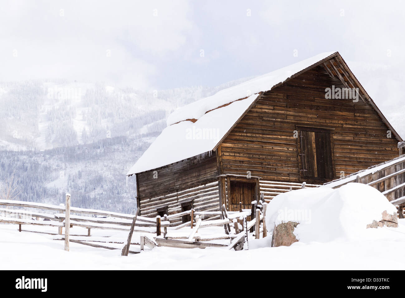 Aged barn on snowy hillside with ski lifts and ski slopes in background ...